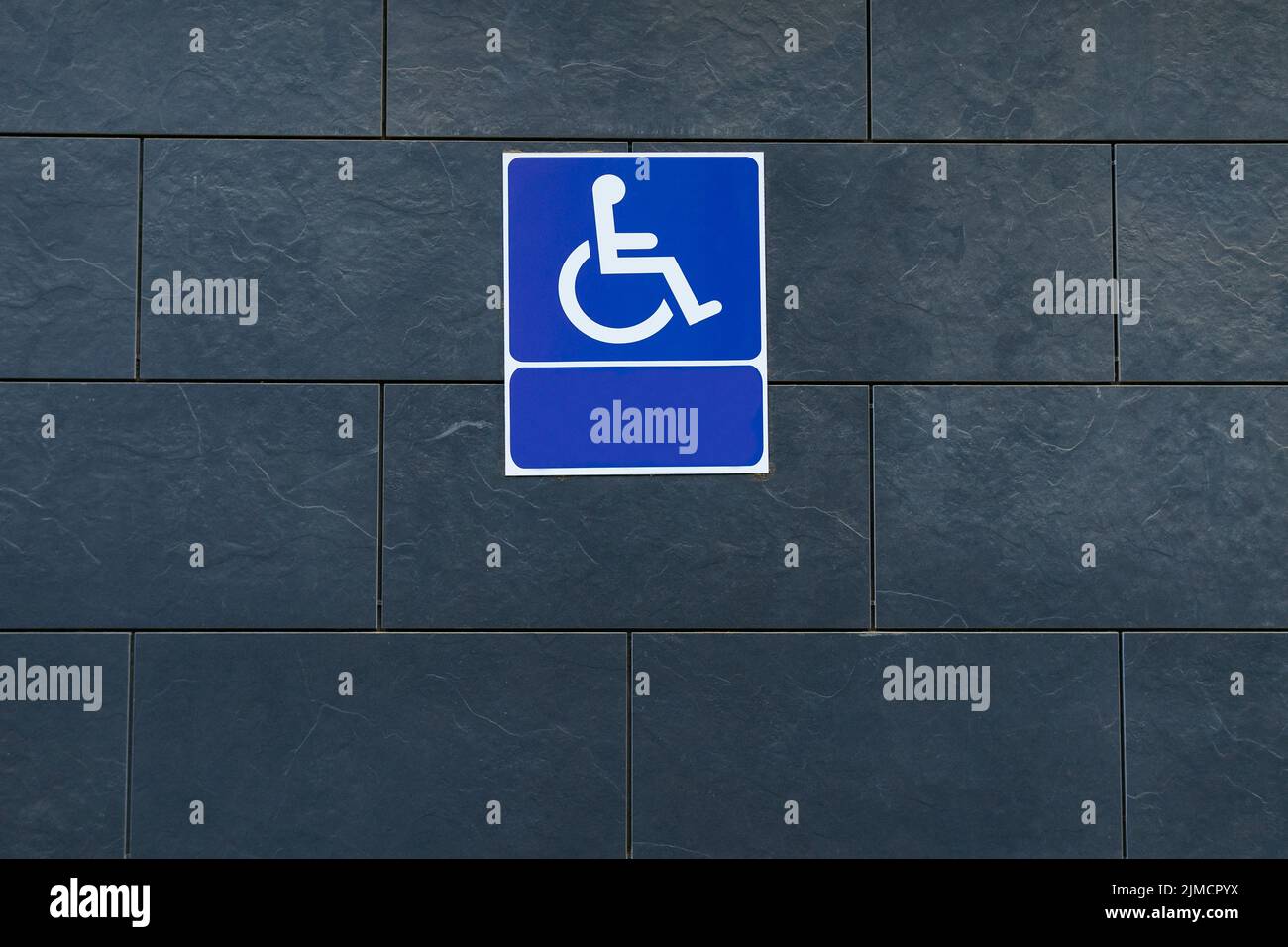 Blue accessibility sign attached to dark gray tiled wall of modern ...