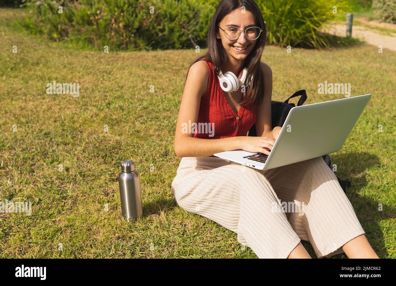 Female student typing on netbook while doing homework on lawn in park ...