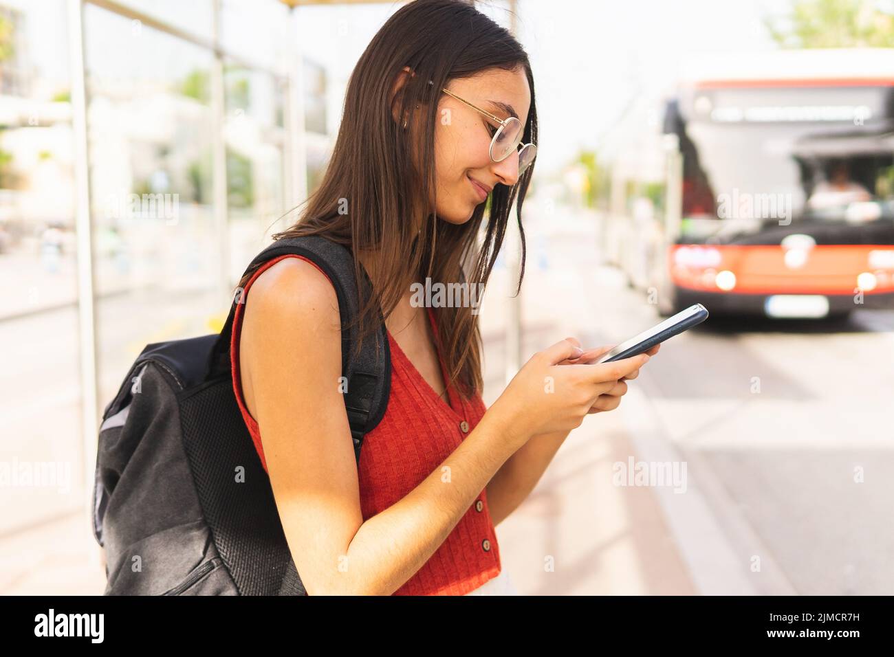 Side view of smiling female student with backpack texting message on ...