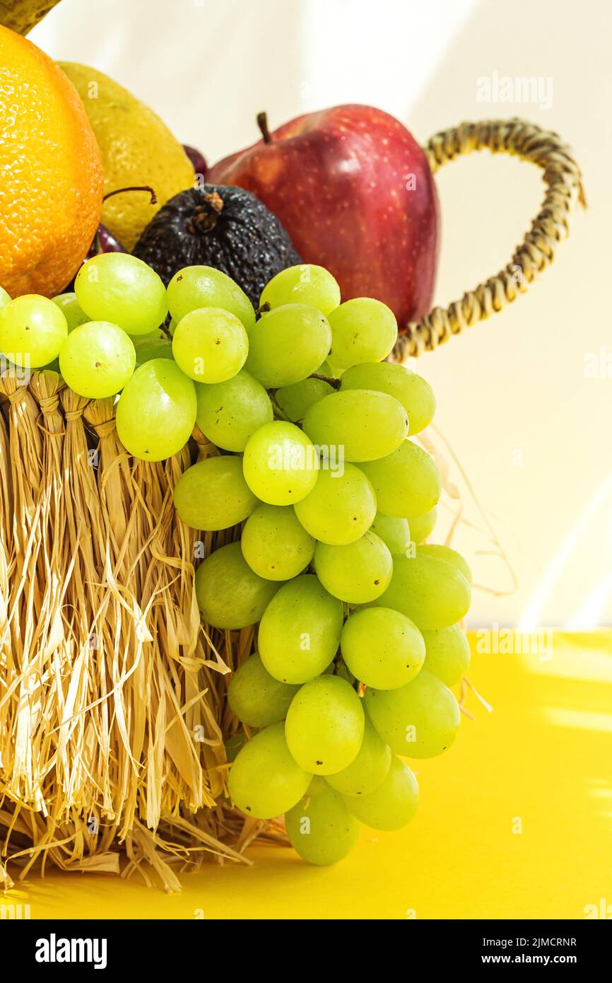 Still life of assorted ripe fruits and grapes placed in wicker basket ...