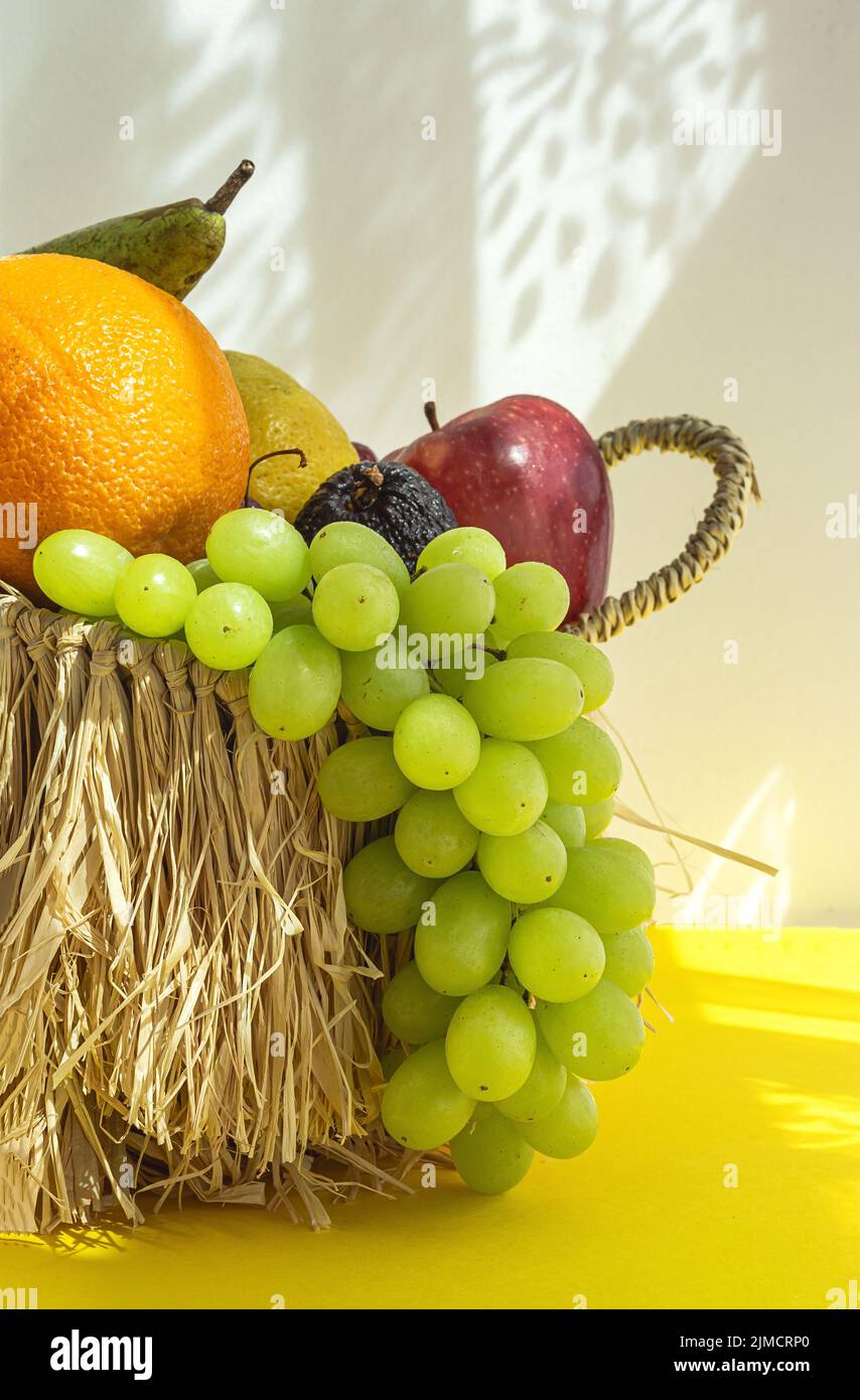 Still life of assorted ripe fruits and grapes placed in wicker basket ...