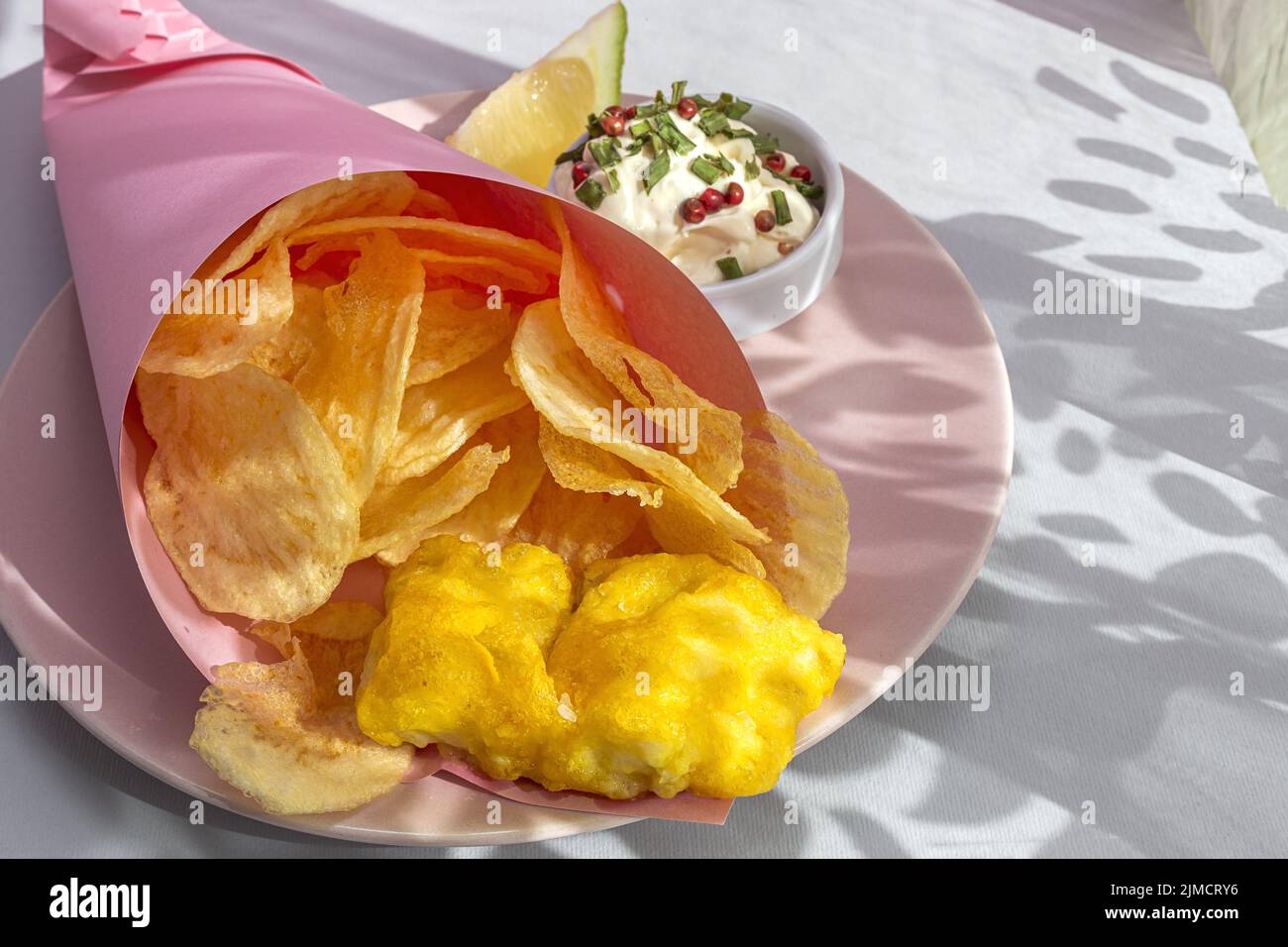 Appetizing fried chips and fish in paper wrapping served on plate with ...