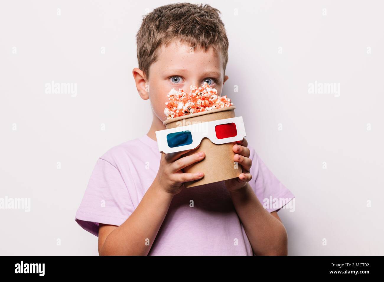 Positive boy looking at camera hiding behind popcorn bucket holding 3D ...