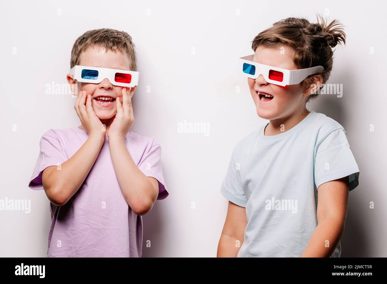 Amazed children in casual wear and 3D glasses touching cheeks with ...