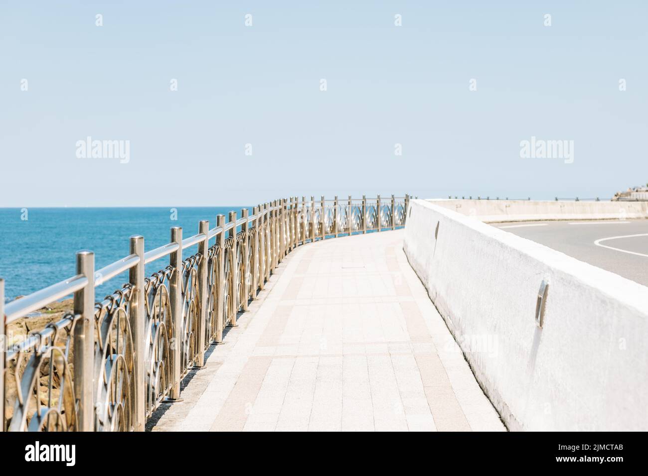 Paved waterfront with long metal fence between rippling endless sea and ...