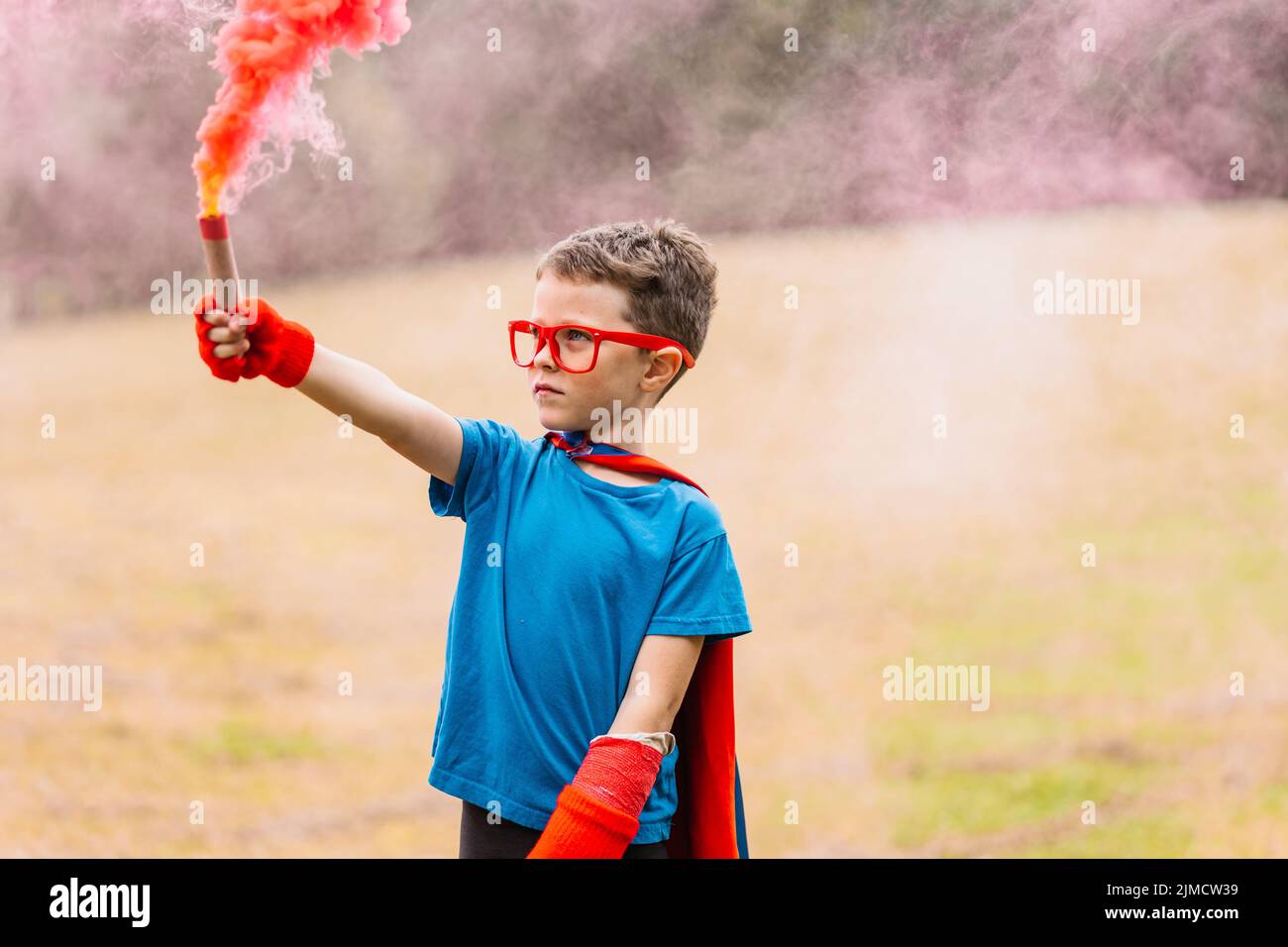 Cute boy in superhero costume and glasses holding red smoke bomb on ...