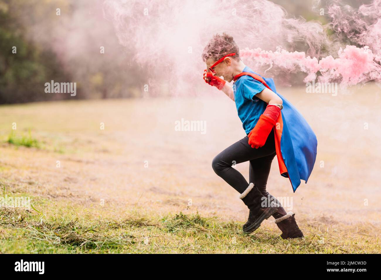 Side view of cute excited boy in superhero costume and glasses holding ...