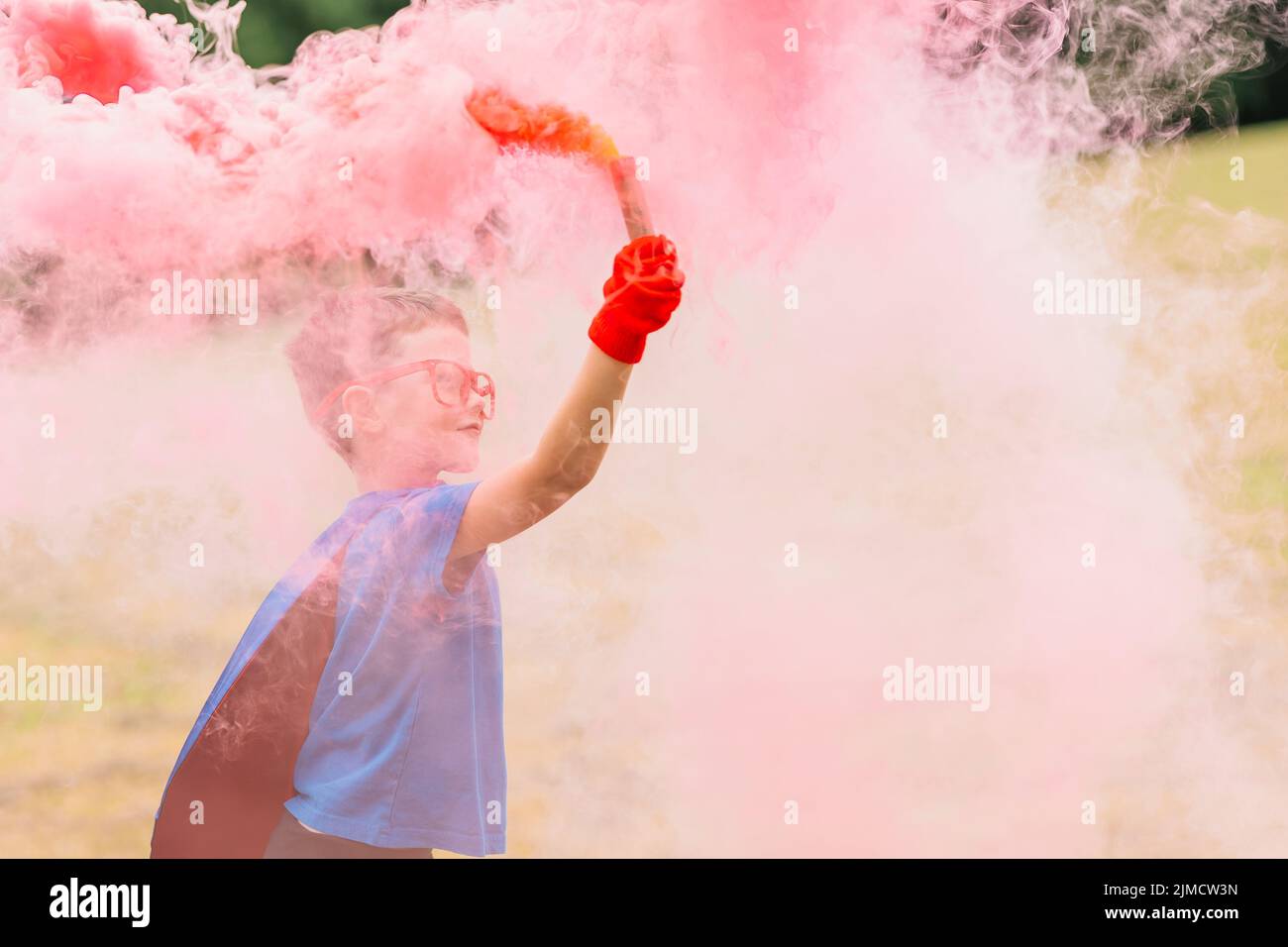 Side view of cute boy in superhero costume and glasses holding red ...