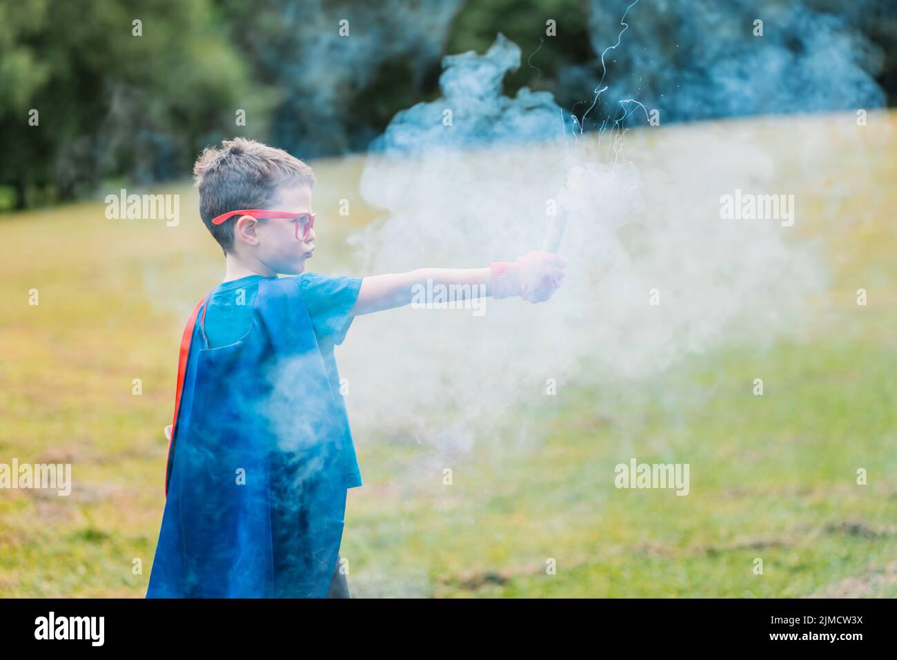 Cute boy in superhero costume and glasses holding smoke bomb on blurred ...