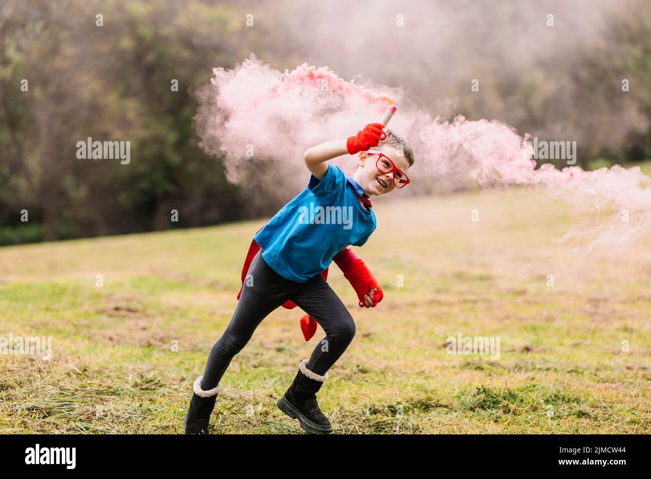Cute excited boy in superhero costume and glasses holding red smoke ...