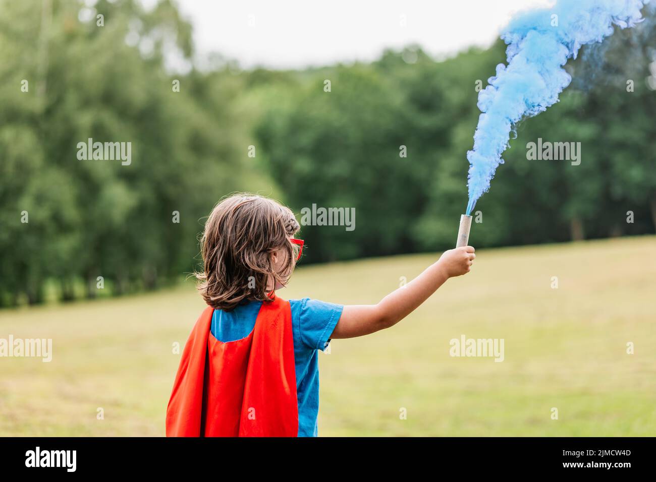 Side view of girl in superhero costume waving hand with blue smoke bomb ...