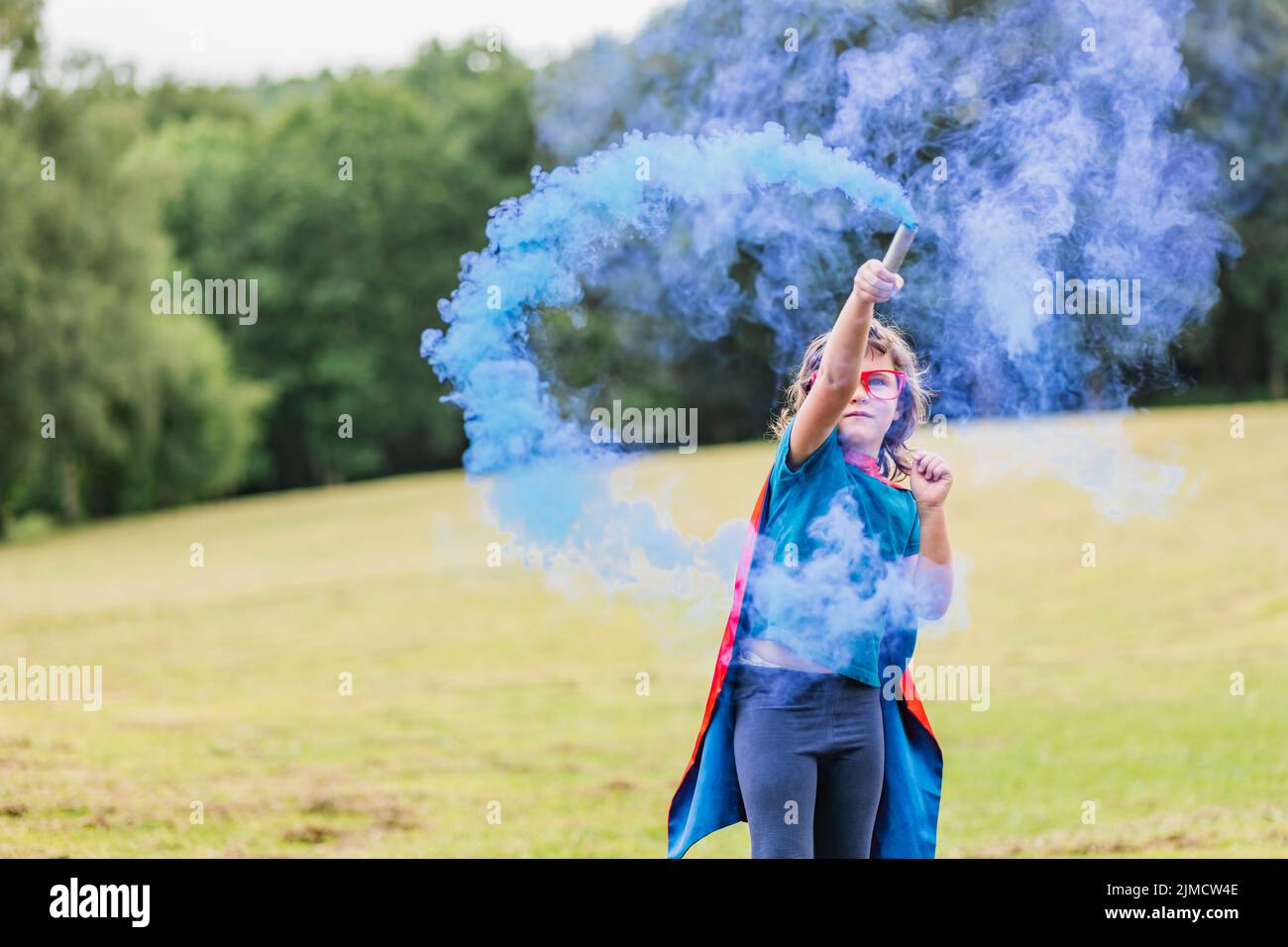 Girl in superhero costume waving hand with blue smoke bomb while ...