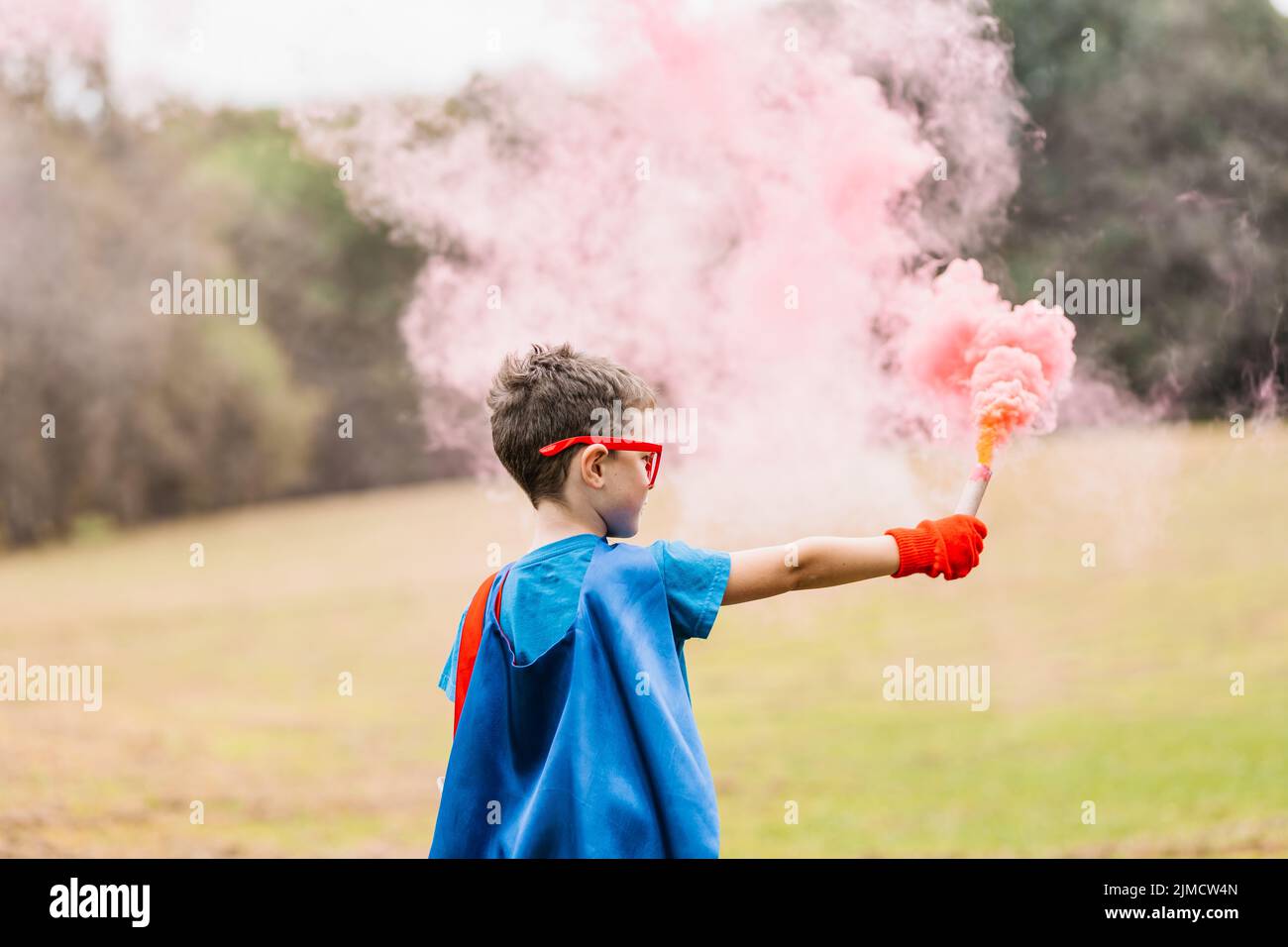Side view of cute boy in superhero costume and glasses holding red ...
