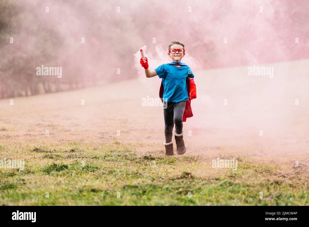 Cute excited boy in superhero costume and glasses holding red smoke ...