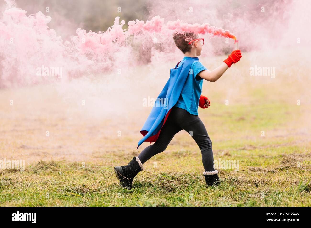 Side view of cute excited boy in superhero costume and glasses holding ...