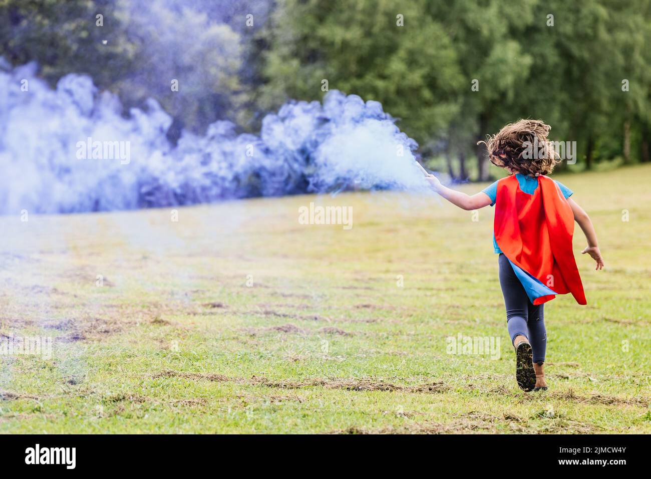 Back view of cute excited girl in superhero costume and glasses holding ...