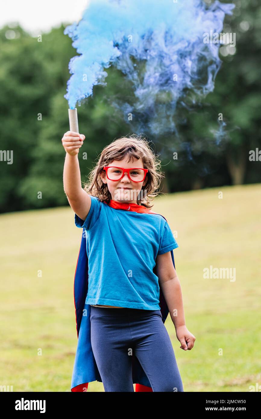 Girl in superhero costume waving hand with blue smoke bomb while ...