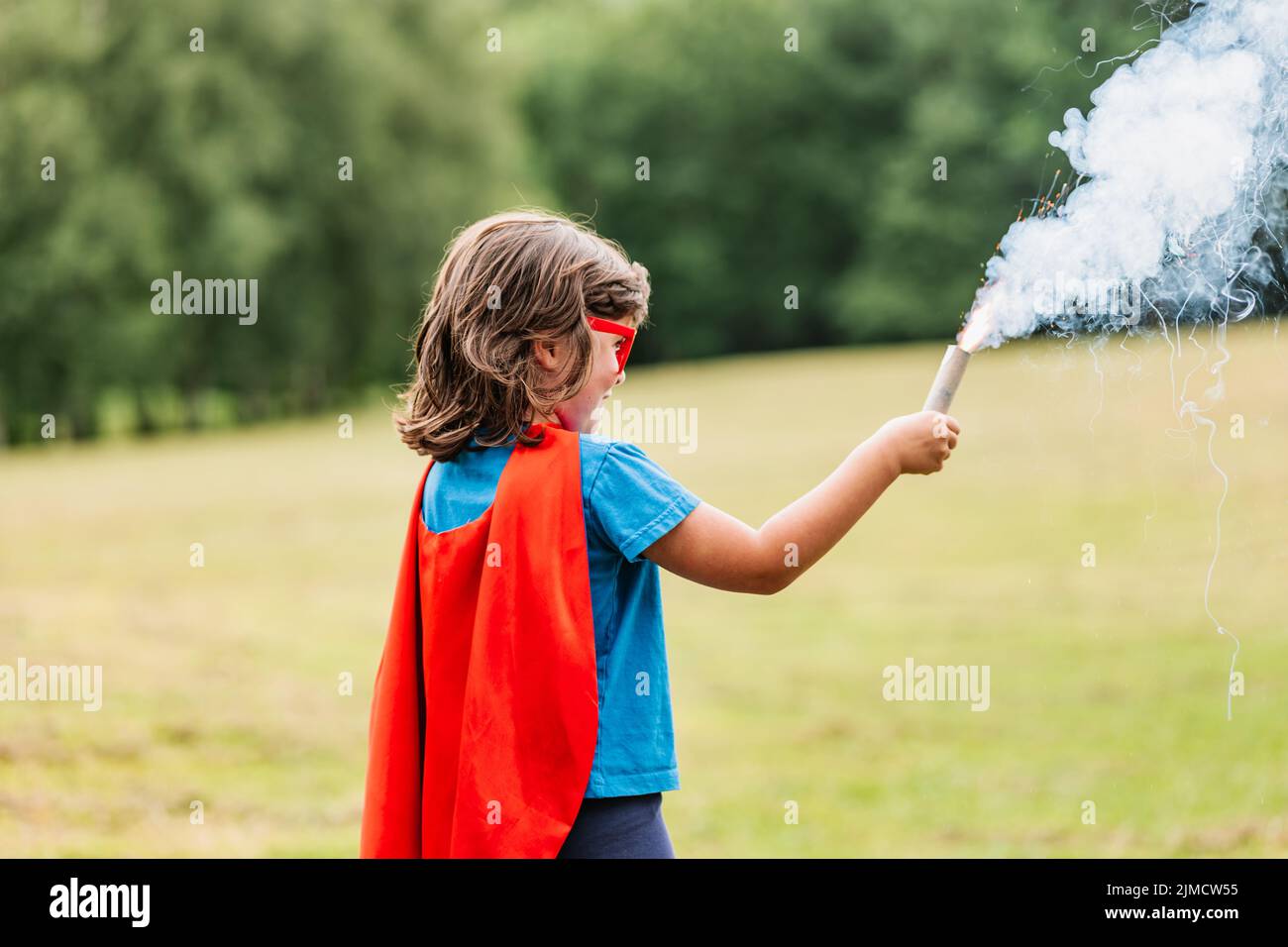 Side view of girl in superhero costume waving hand with blue smoke bomb ...