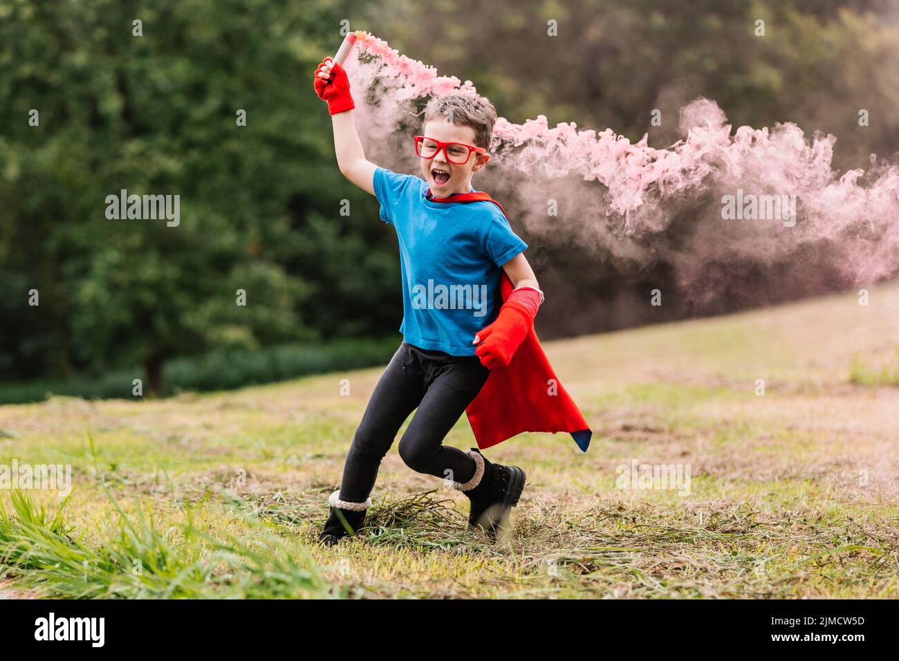 Cute excited boy in superhero costume and glasses holding red smoke ...