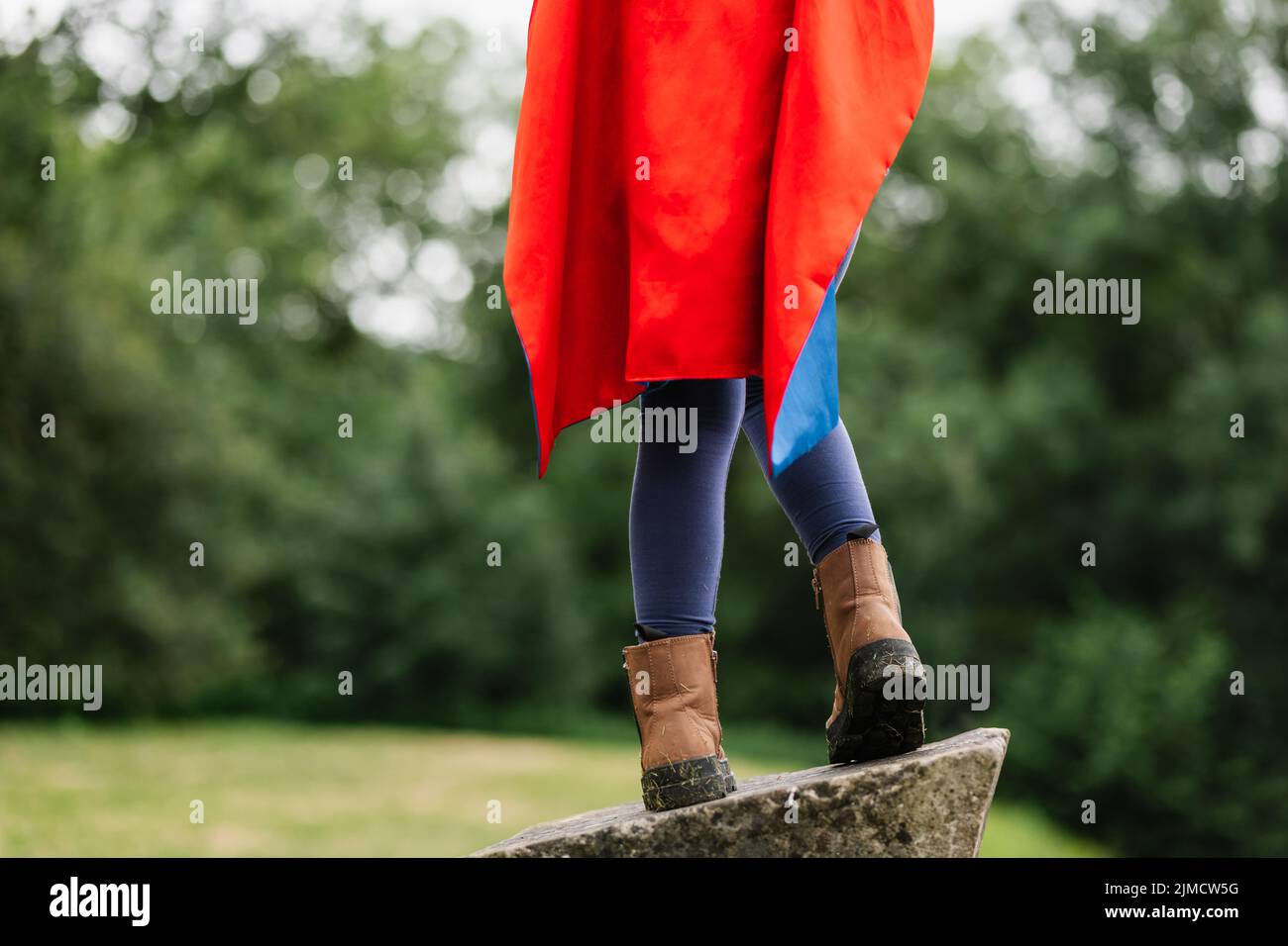 Anonymous child in red cape standing on rock structure on blurred ...
