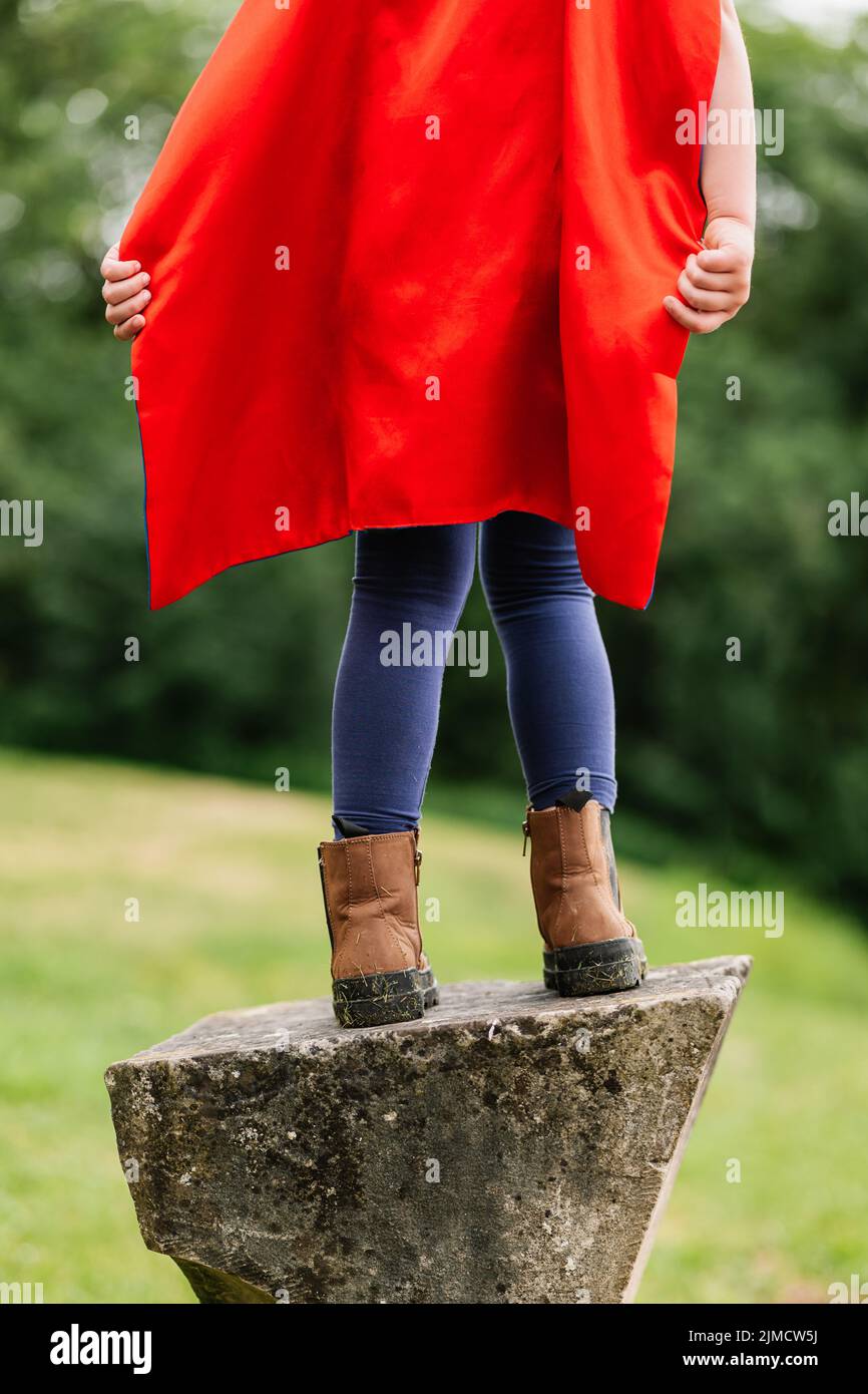Anonymous child in red cape standing on rock structure on blurred ...