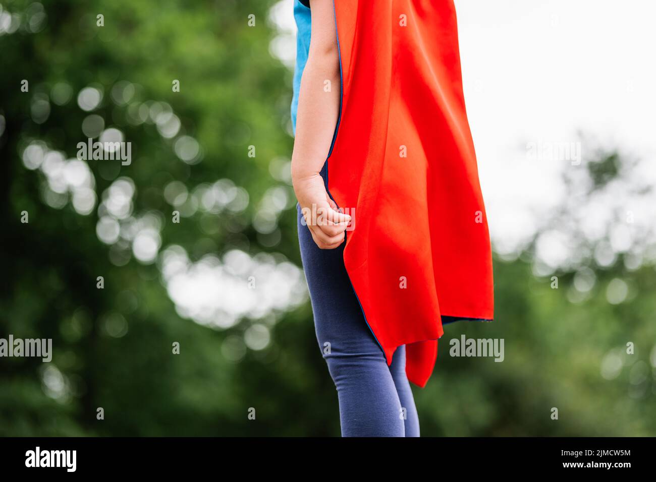 Anonymous child in red cape standing on rock structure on blurred ...