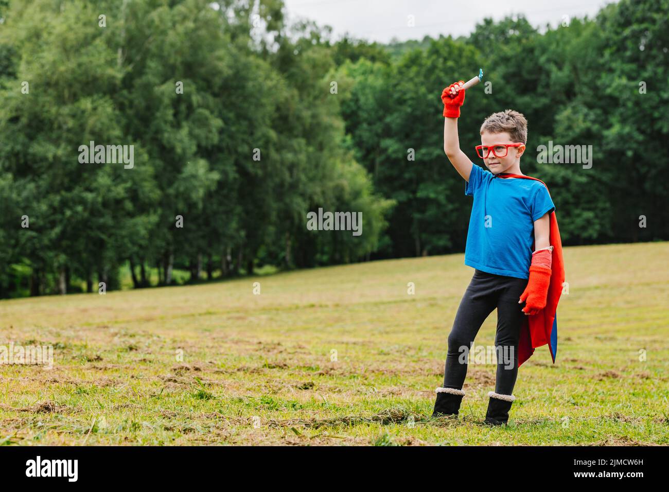 Smiling boy in superhero costume and glasses holding red smoke bomb on ...