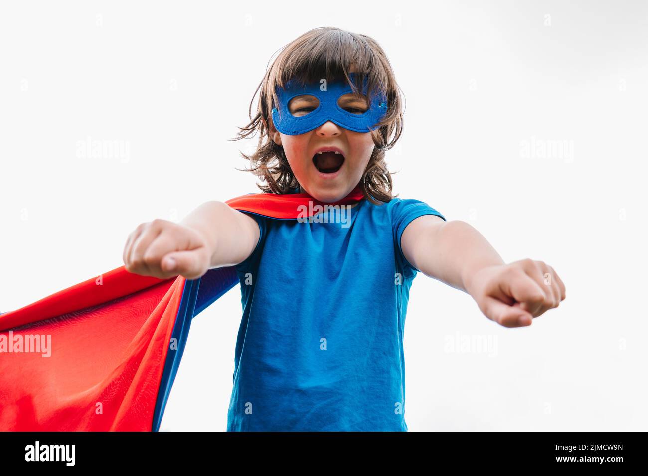 Low angle of powerful girl with cape and mask clenching fists and ...