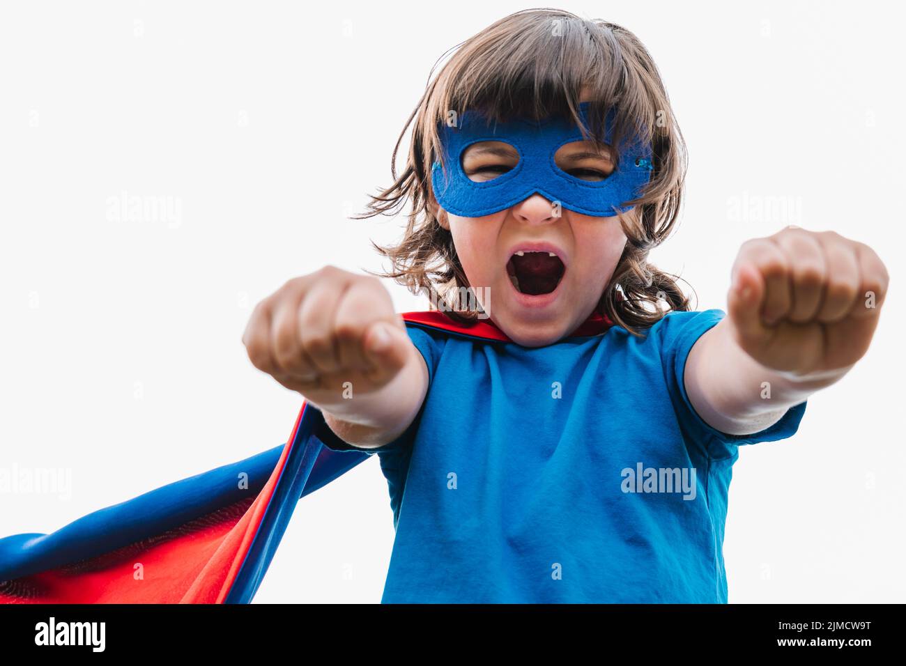 Low angle of powerful girl with cape and mask clenching fists and ...