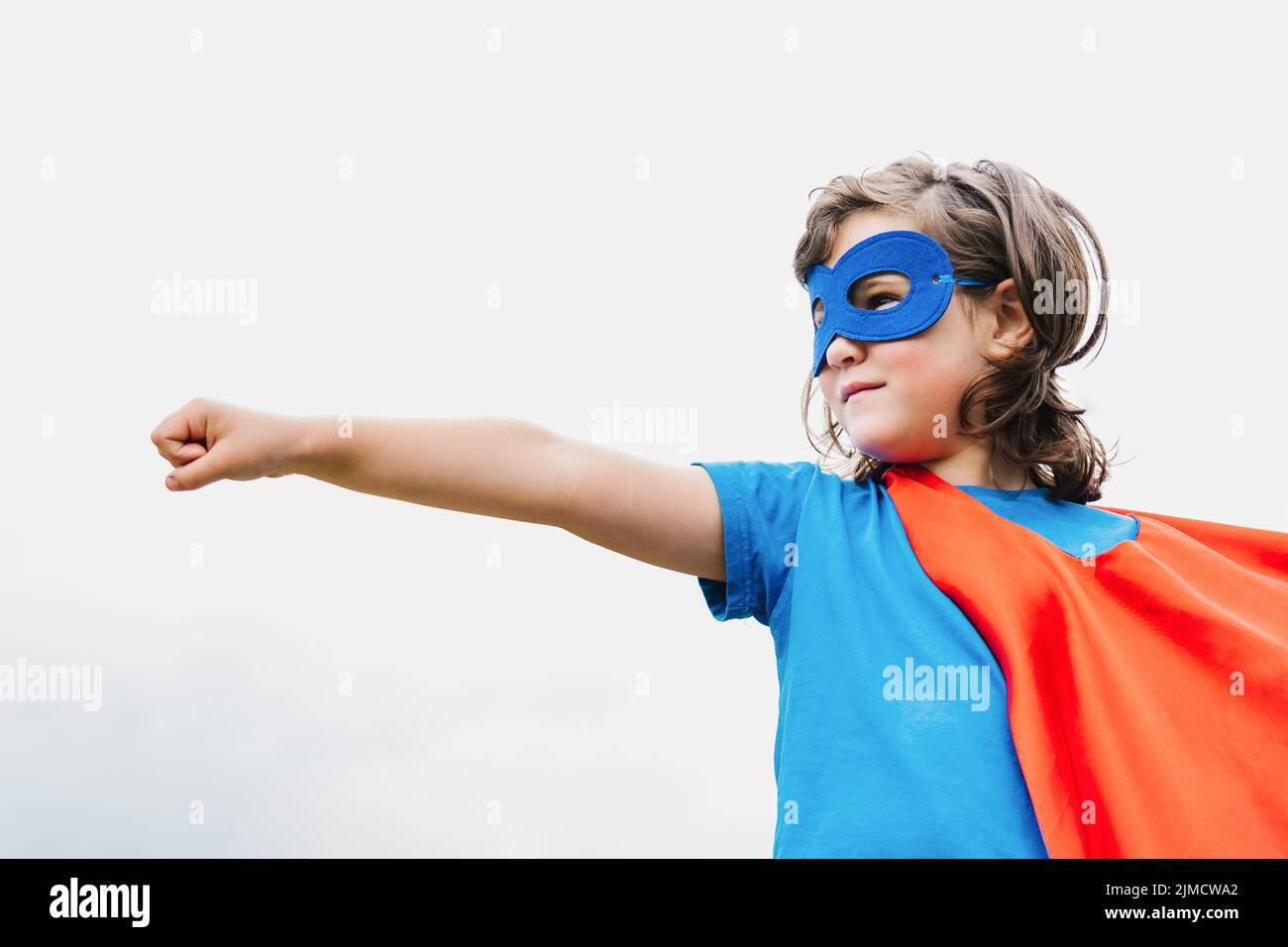 From below side view of little female superhero with cape and mask ...