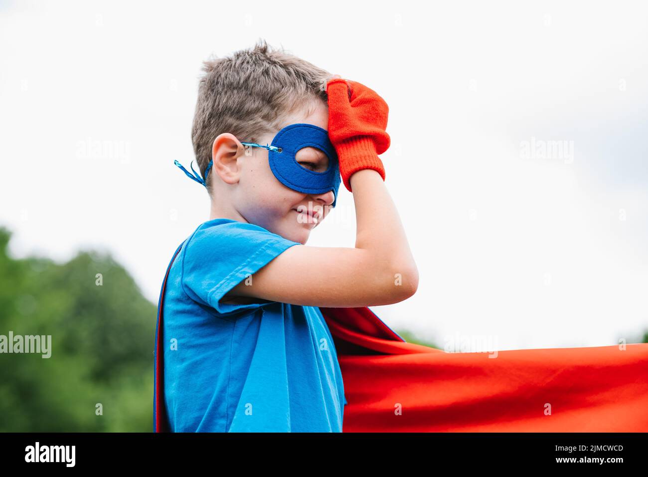 From below little superhero with cape and mask raising arm with ...