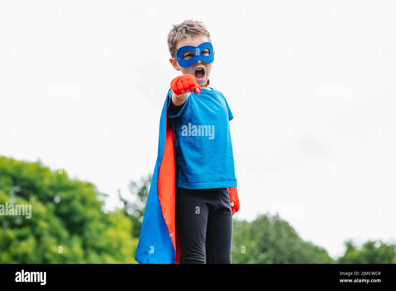 Little superhero with cape and mask raising arm with clenched fist and ...