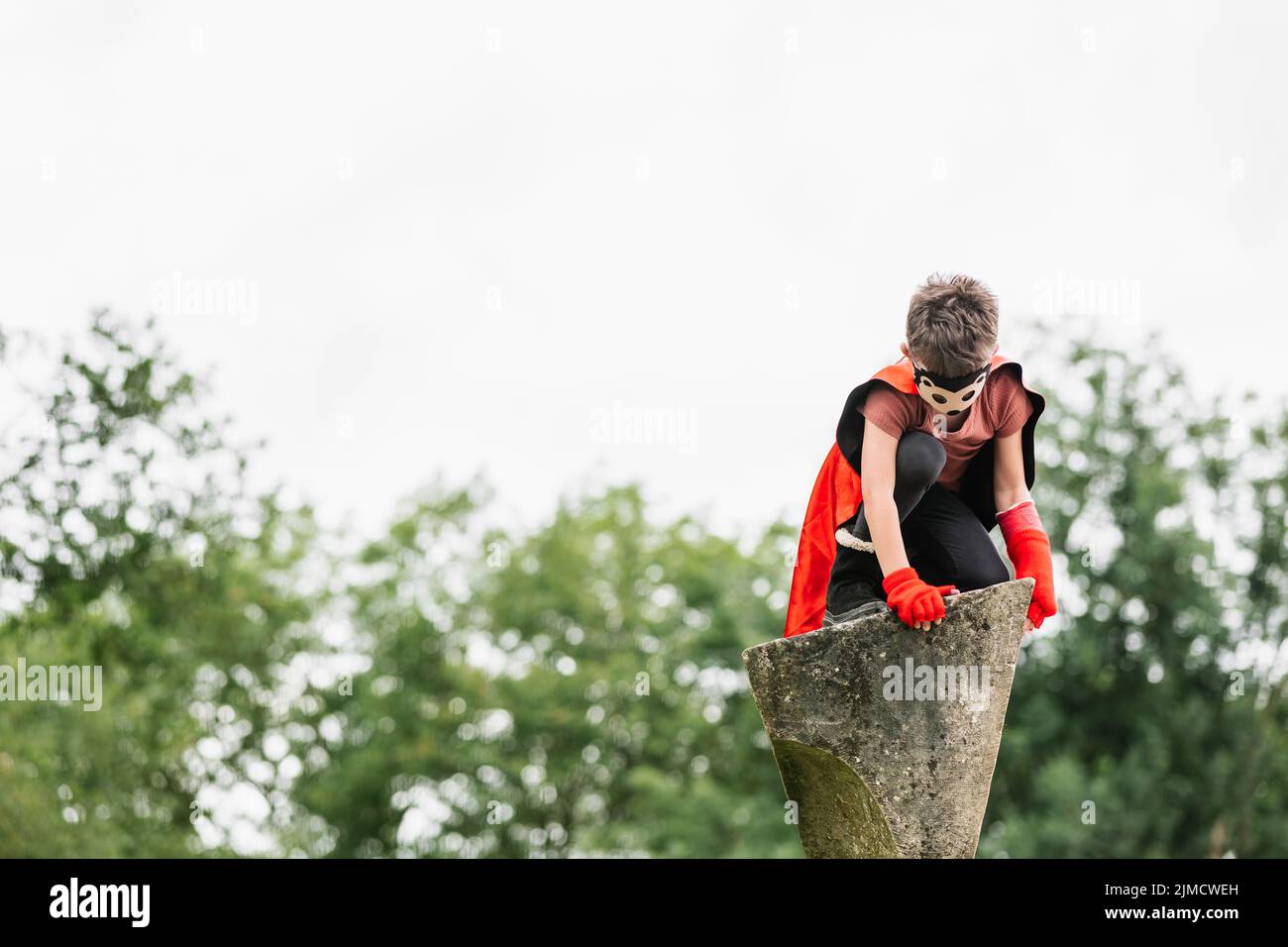 From below boy in red superhero cape and hedgehog mask looking down ...