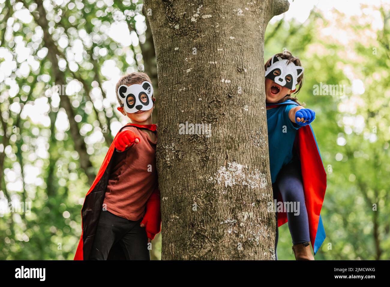 Brother and sister in superhero capes and animal masks hiding behind ...