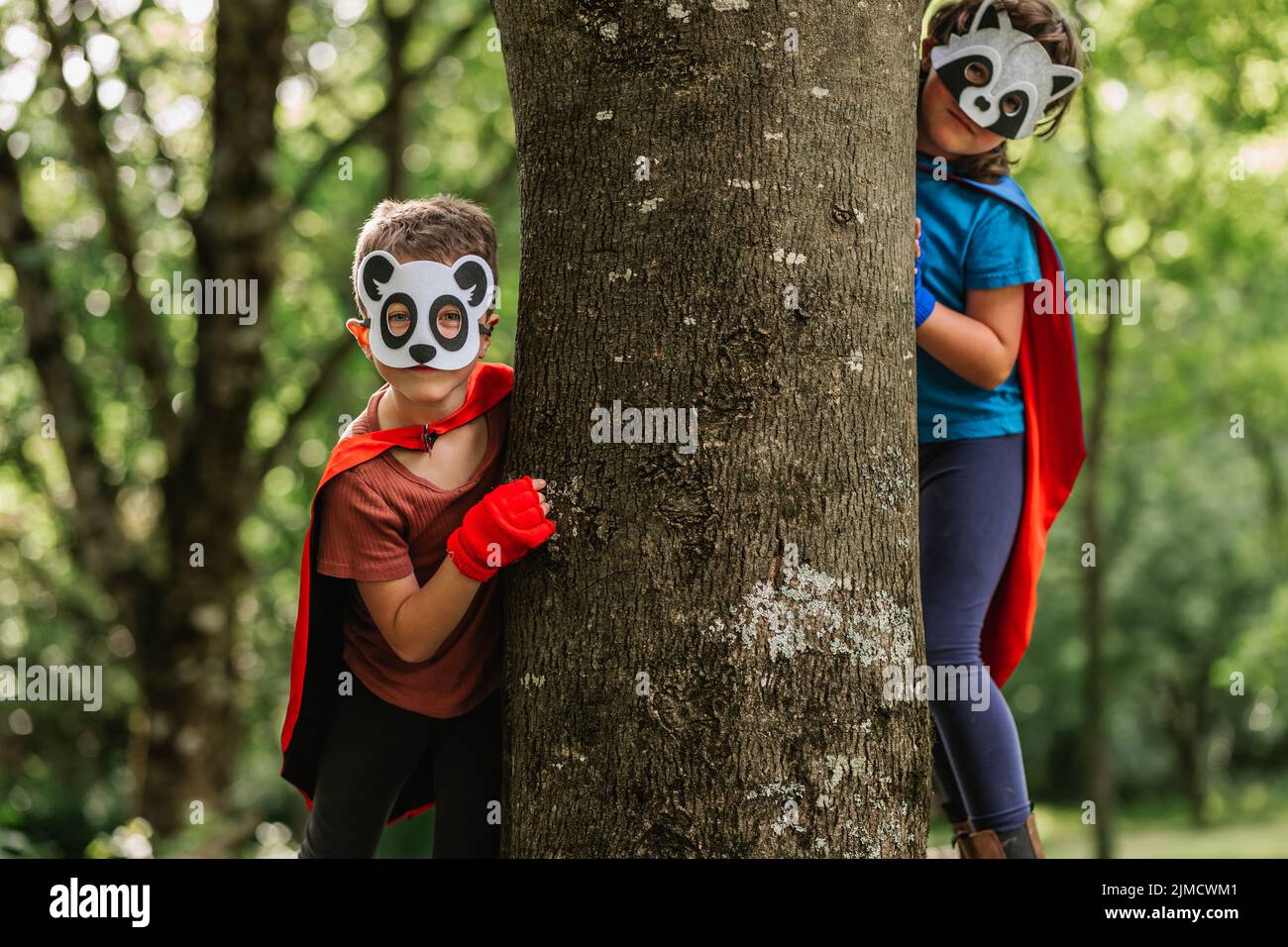 Brother and sister in superhero capes and animal masks hiding behind ...