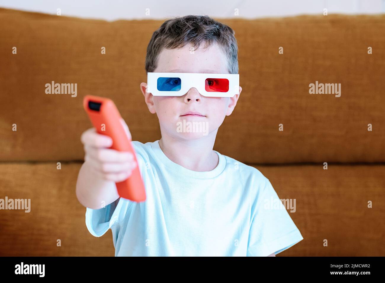 Focused child in colorful 3D glasses changing channels with remote ...