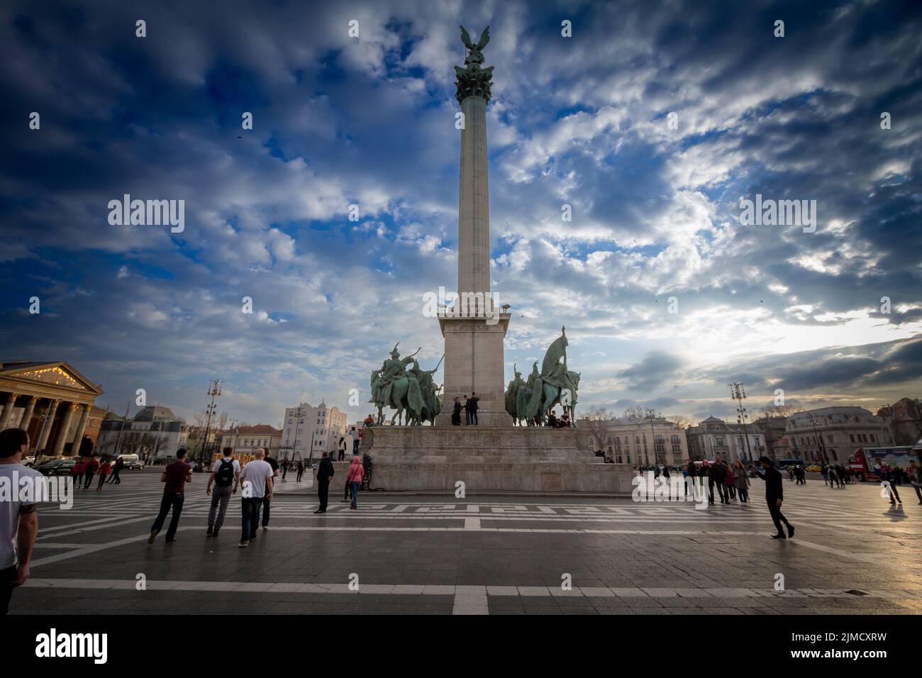 Picture of people walking by the main column of Heroes Square at sunset. Hosok tere (English ...