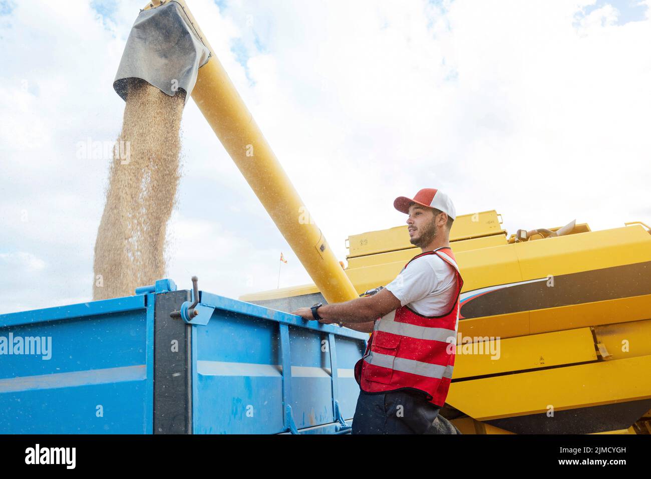 Side view of male farmer standing near industrial combine harvester ...