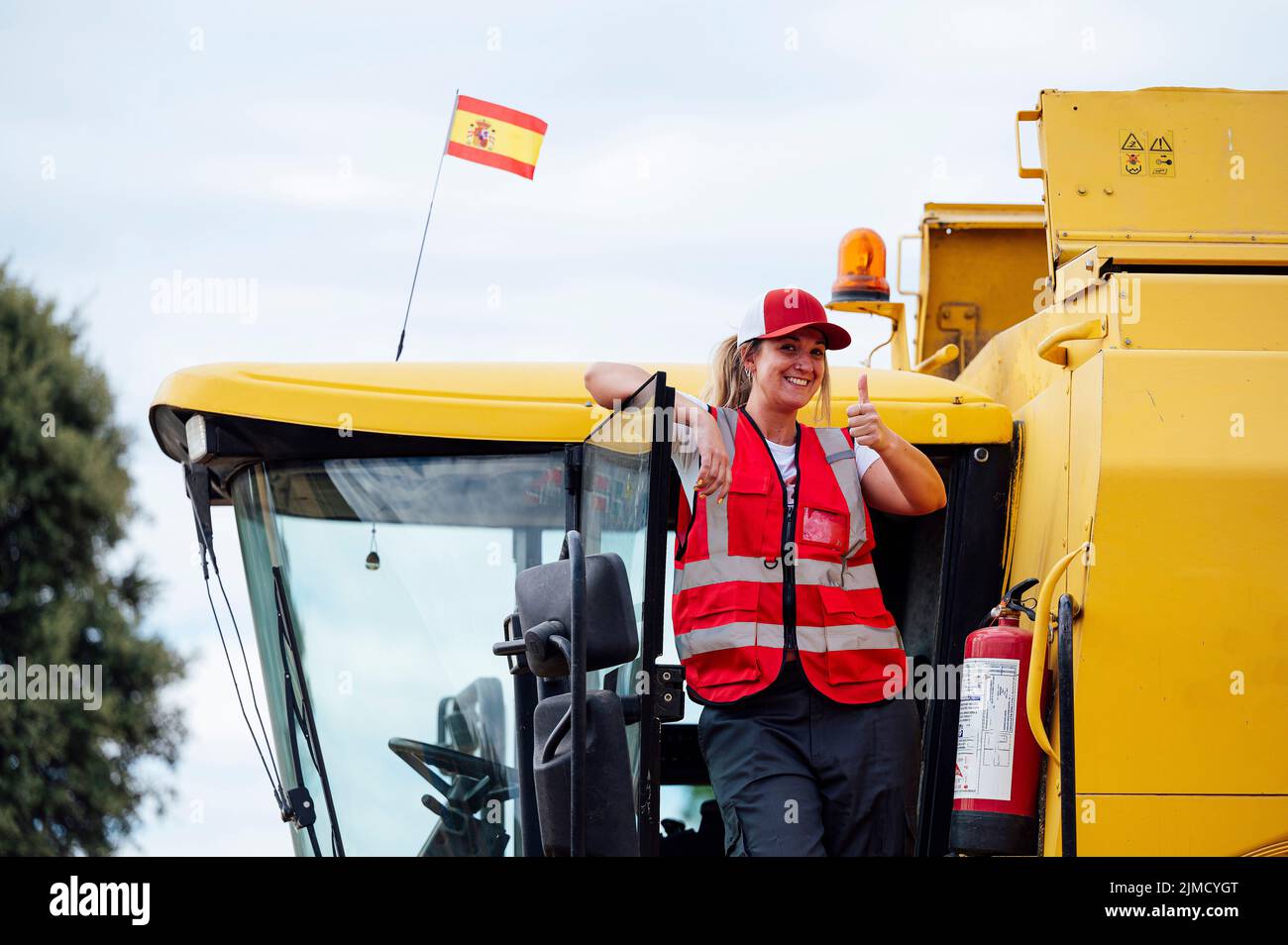 Positive female combine operator in uniform showing thumb up gesture ...