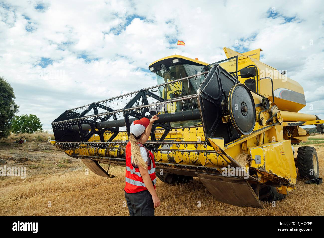Back view of anonymous female worker in uniform examining combine ...