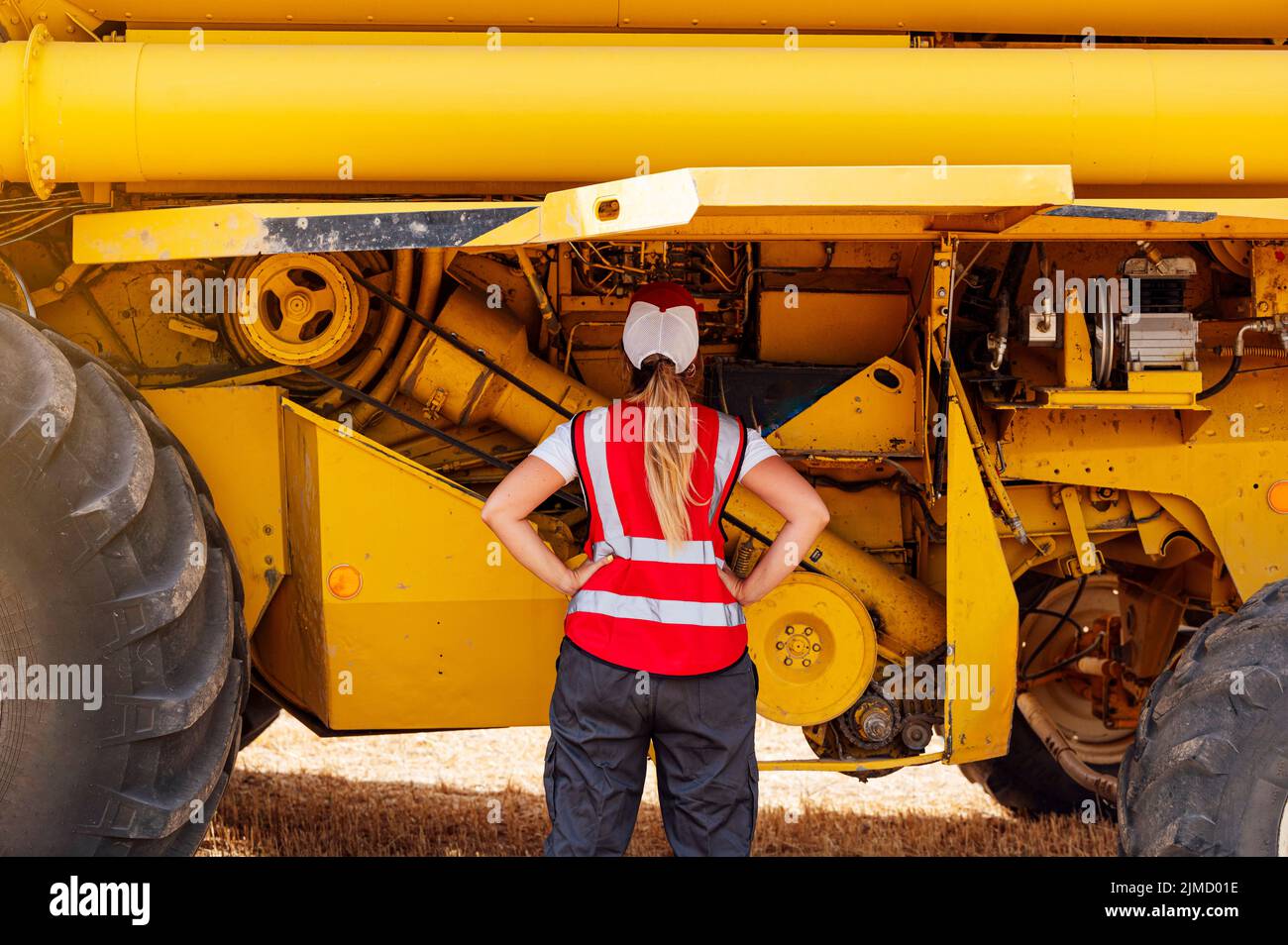 Back view of anonymous female worker in uniform examining combine ...
