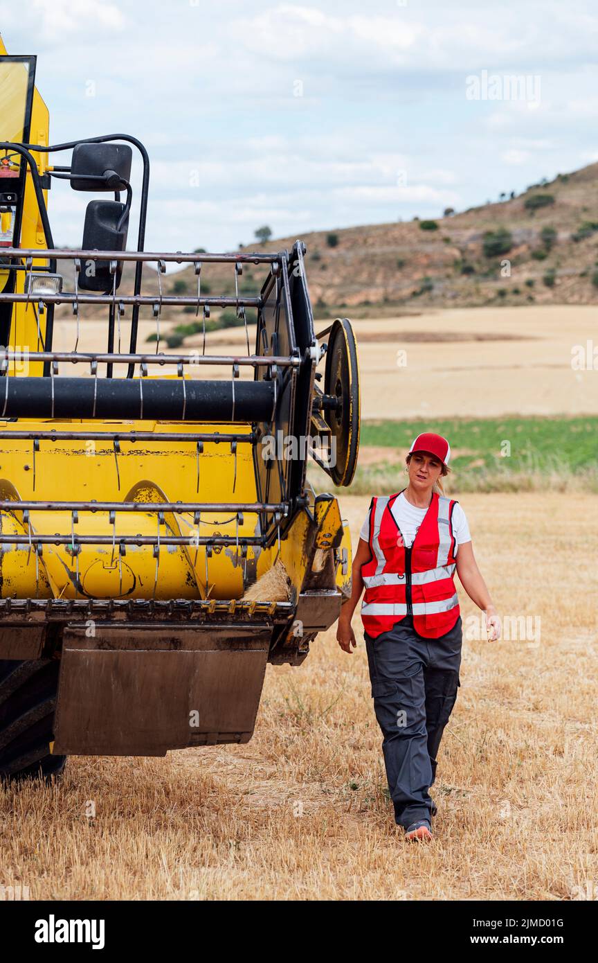 Female worker in uniform examining combine harvester while working in ...