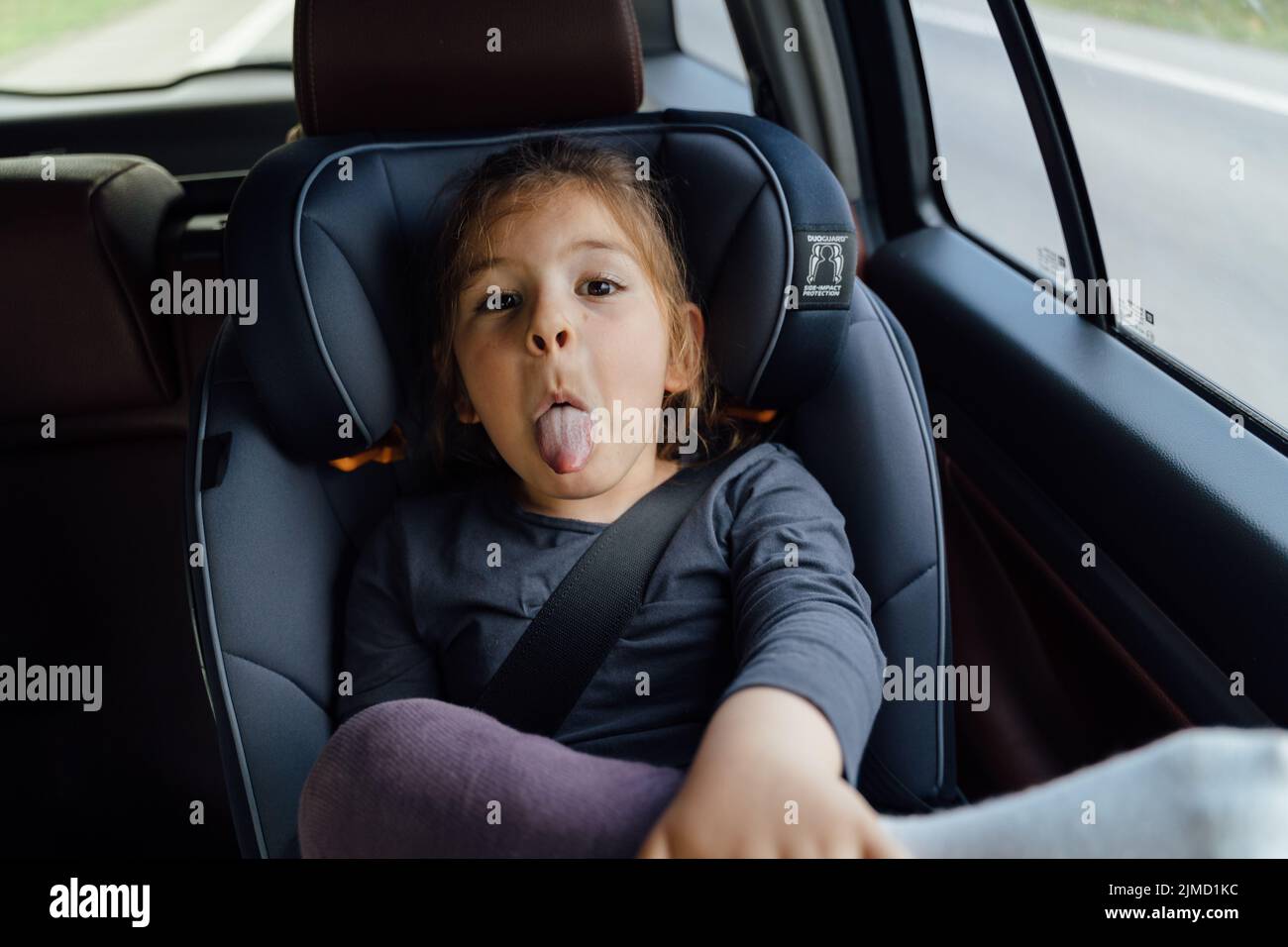 Funny adorable little girl sticking tongue out while sitting in car ...