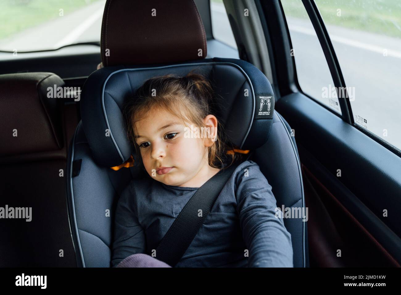 Thoughtful adorable tired little girl resting while sitting in car seat ...