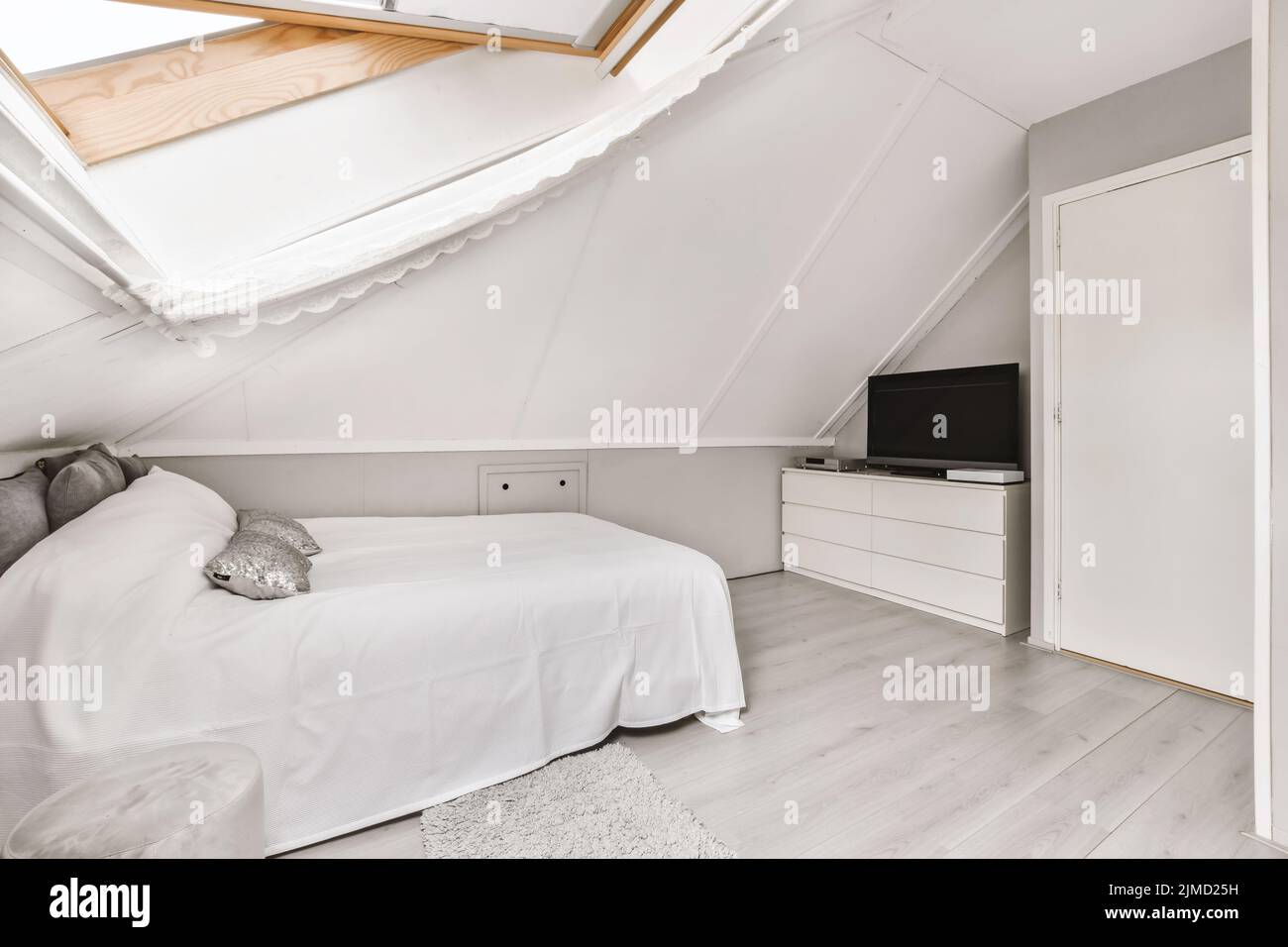 Comfortable bed with white walls next to a small furniture with a tv ...