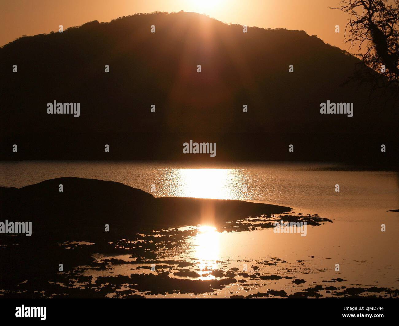 Sunsets with lens flare over mountain and glistening on lake below in ...