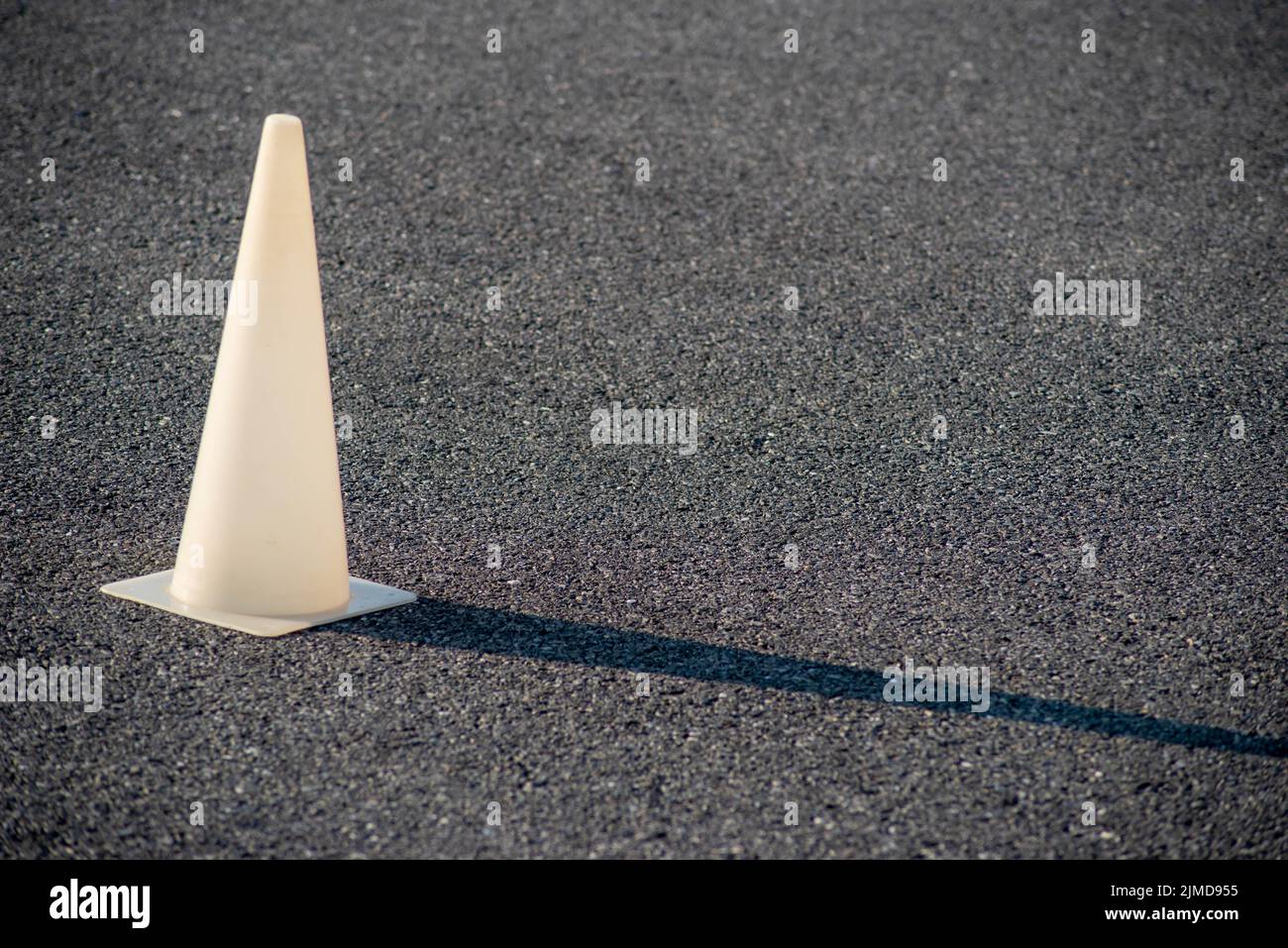 White traffic cone casts a long shadow across dark asphalt Stock Photo ...