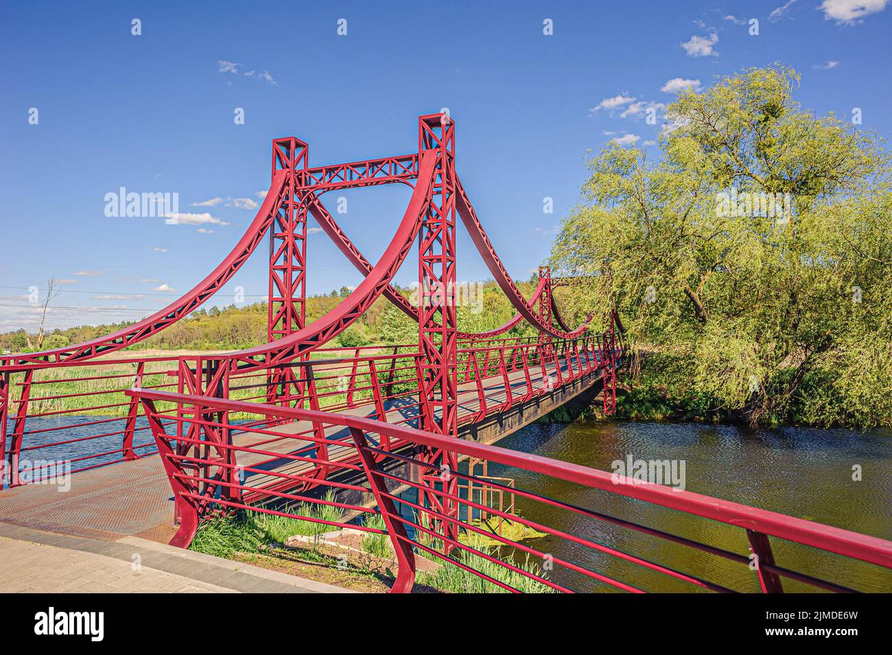 Beautiful iron red suspension pedestrian bridge over the small river ...