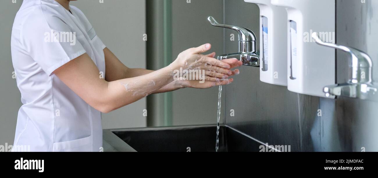 The doctor washes his hands under the tap in a stainless steel sink ...