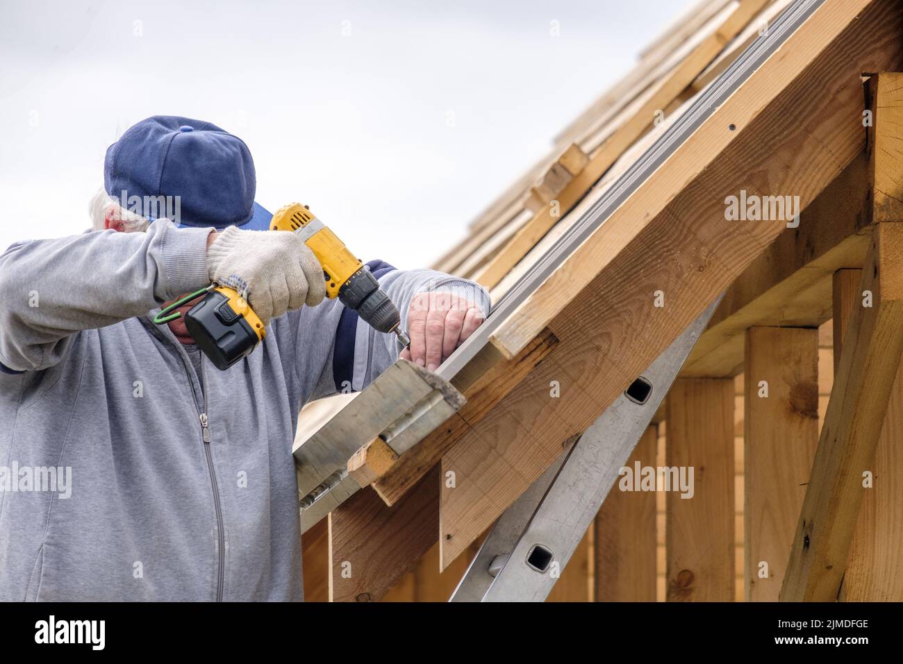 Senior builder man with a screwdriver screwing a roofing sheet to the ...
